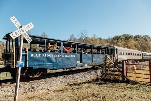 A blue train labeled "Blue Ridge Scenic Railway" passes a railroad ...